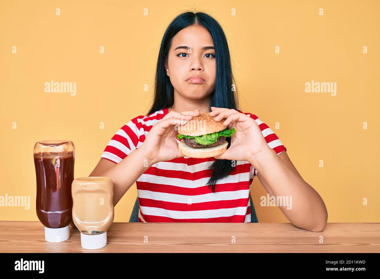 Young asian girl eating a tasty classic burger depressed and worry for ...