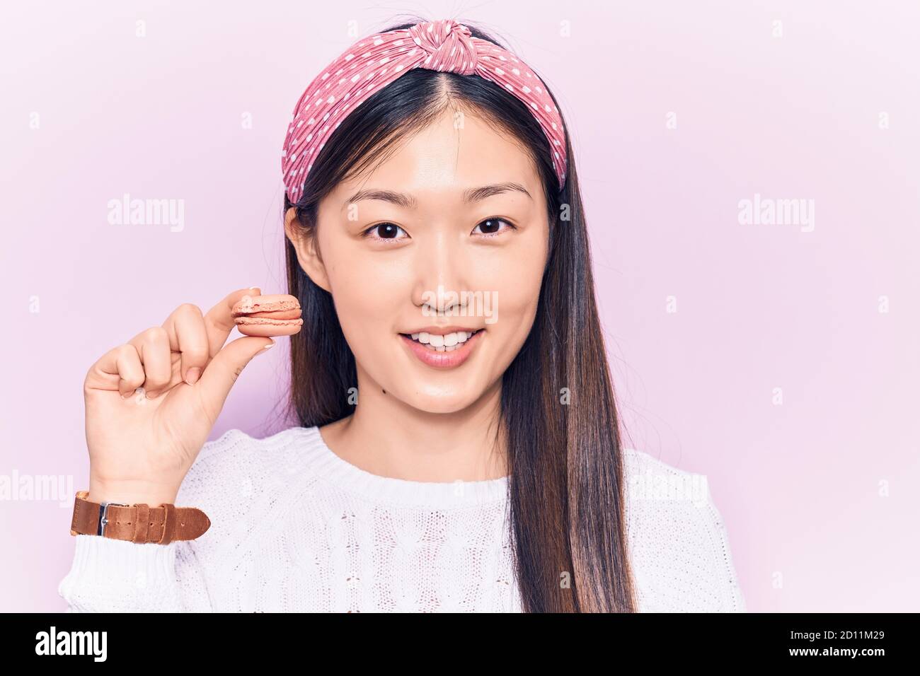 Young beautiful chinese woman hoding french dessert macaron looking ...