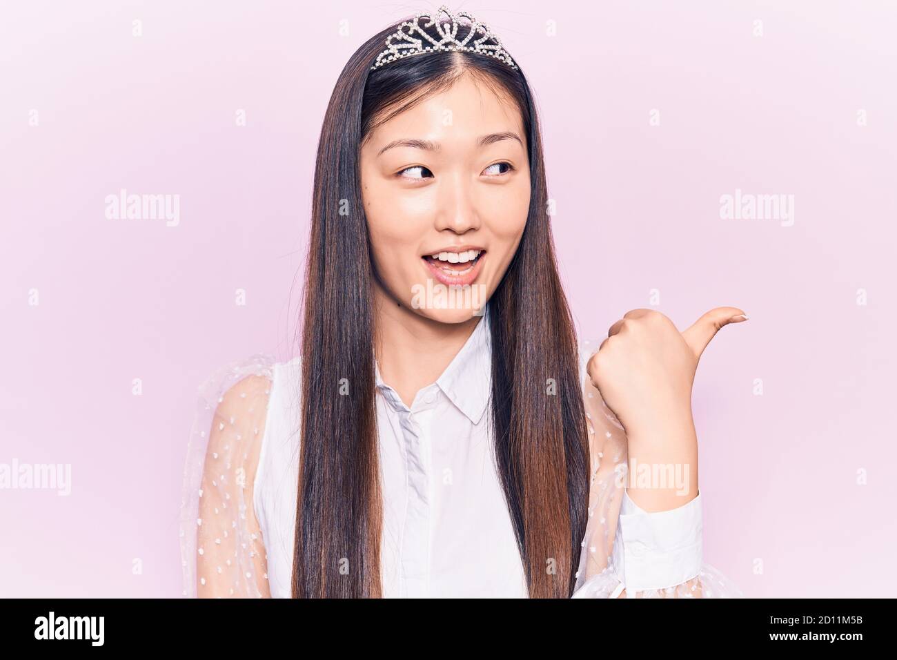 Young beautiful chinese woman wearing princess crown pointing thumb up ...