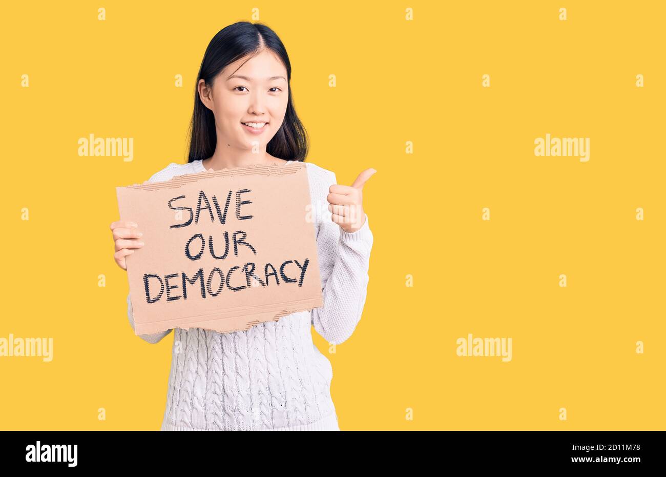 Young beautiful chinese woman holding save our democracy cardboard ...