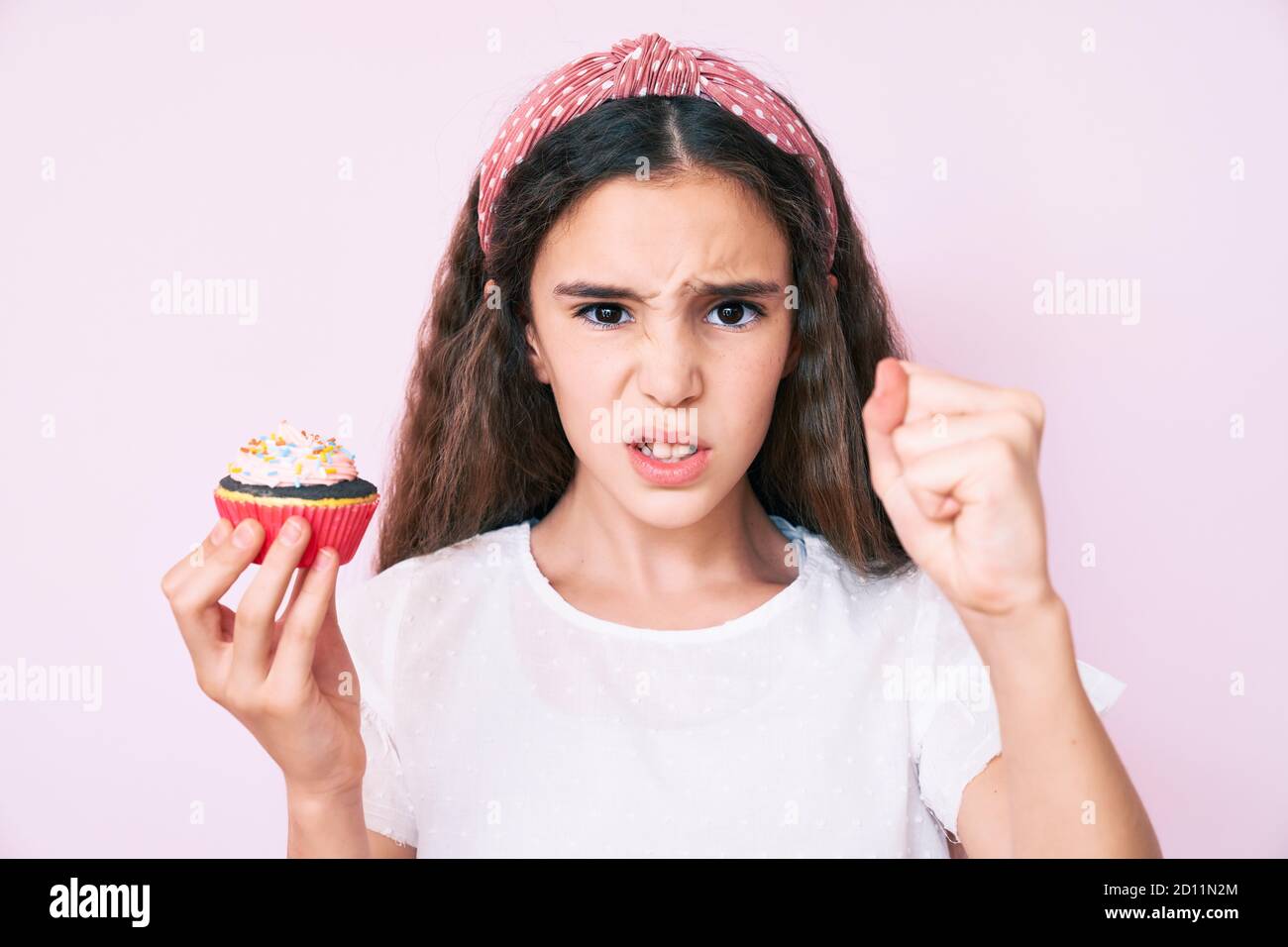 Cute hispanic child girl holding cupcake annoyed and frustrated ...