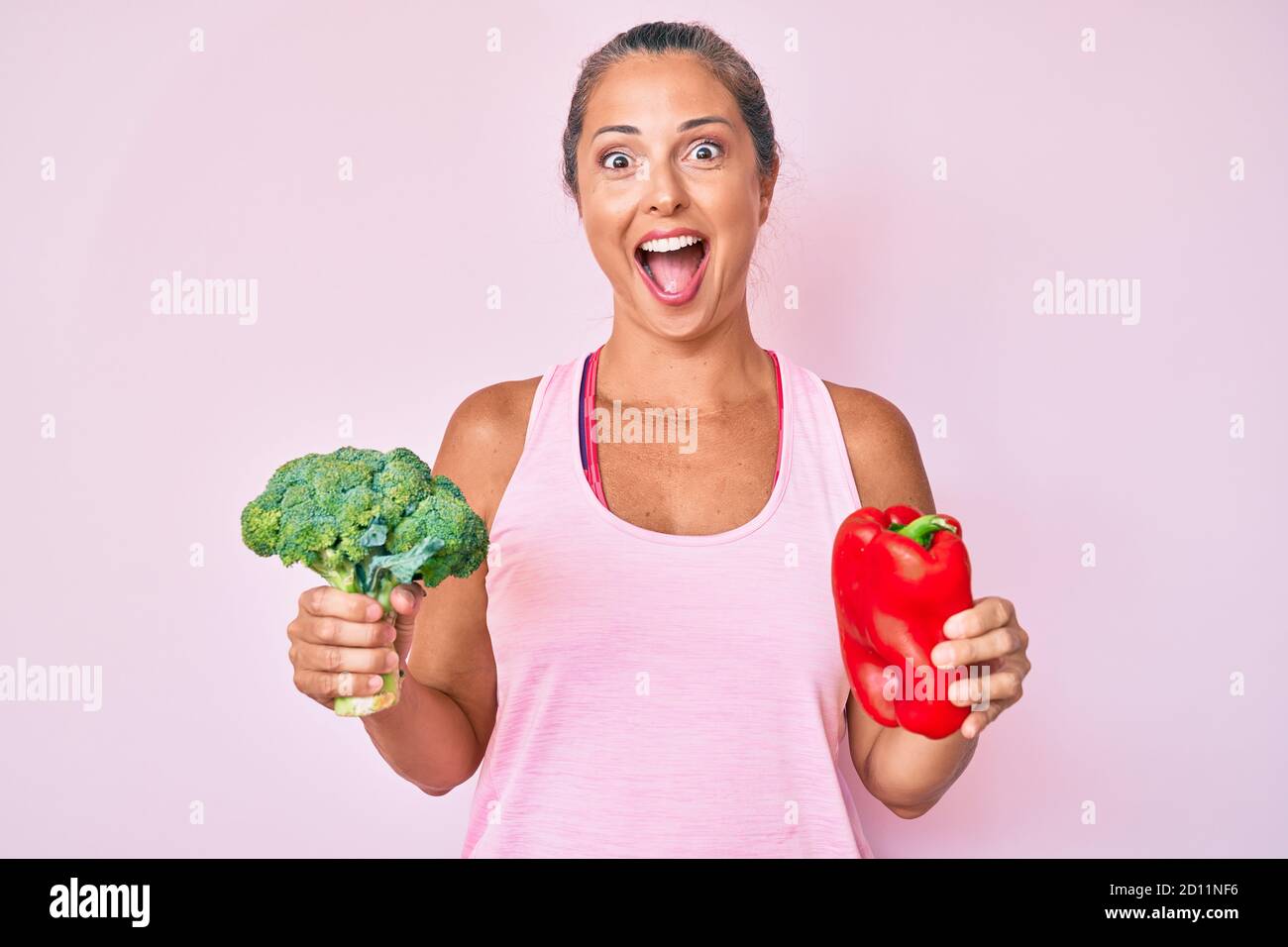 Middle age hispanic woman holding broccoli and red pepper celebrating ...