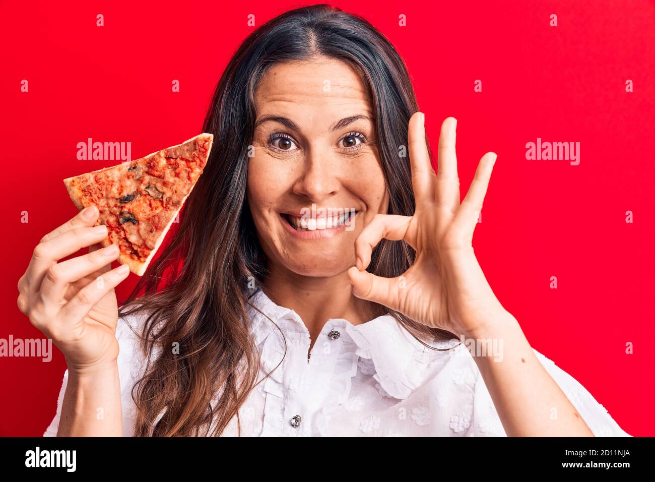 Young beautiful brunette woman eating slice of Italian pizza over isolated red background doing ...