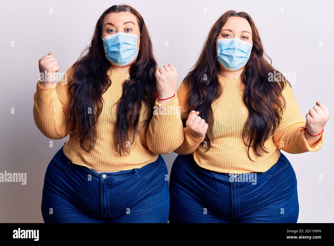 Young plus size twins wearing medical mask celebrating surprised and ...
