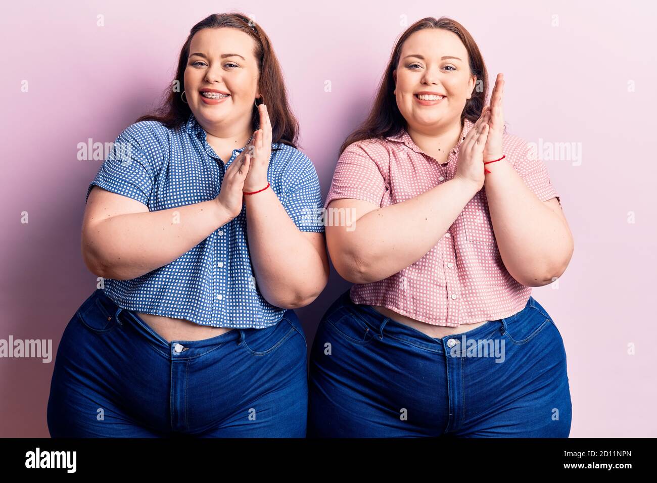 Young plus size twins wearing casual clothes clapping and applauding ...