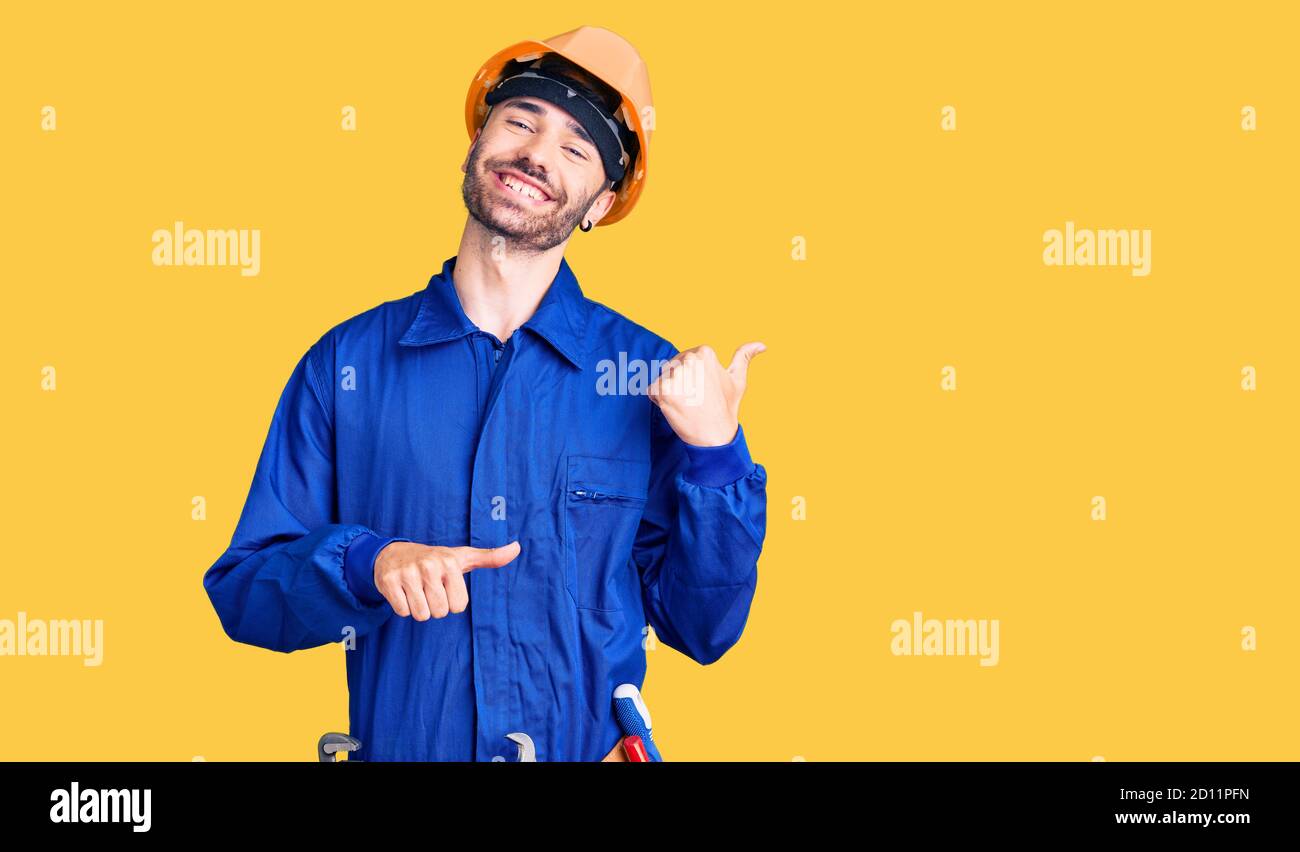 Young hispanic man wearing worker uniform pointing to the back behind ...