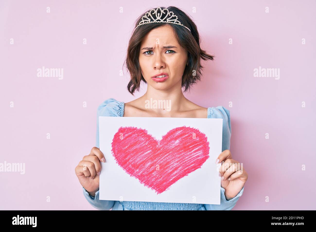 Young beautiful girl wearing princess crown holding heart draw clueless ...