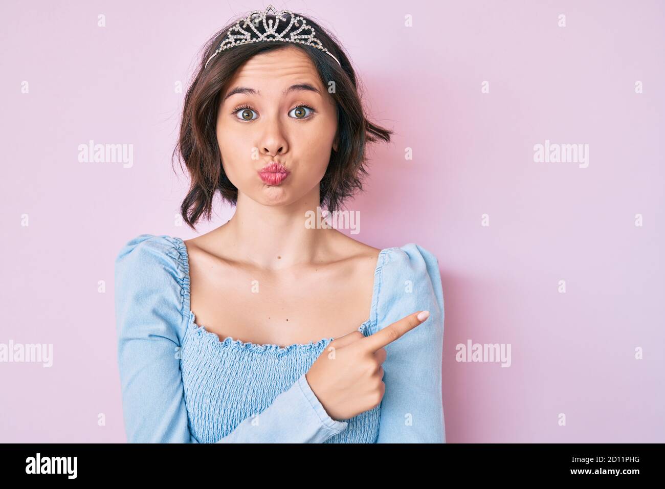 Young beautiful girl wearing princess crown puffing cheeks with funny ...