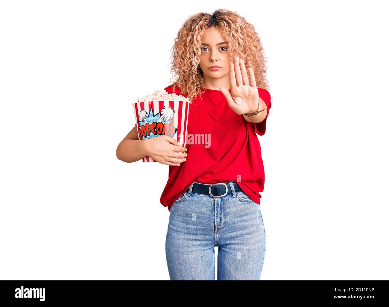 Young blonde woman with curly hair eating popcorn with open hand doing ...