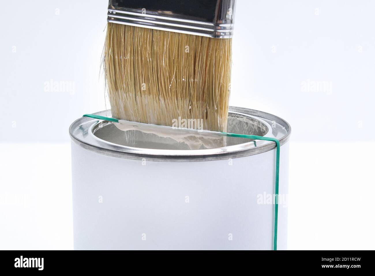 A man removes excess paint from a brush in a can on a white background ...