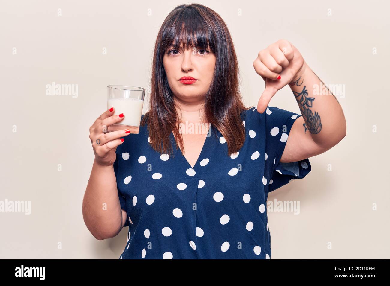 Young plus size woman holding glass of milk with angry face, negative ...