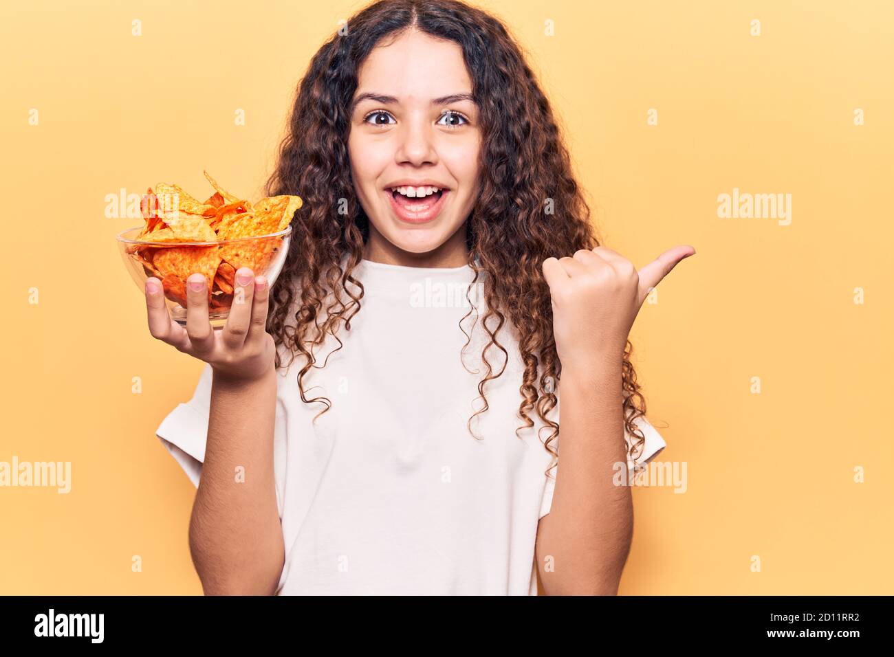 Beautiful kid girl with curly hair holding nachos potato chips pointing ...
