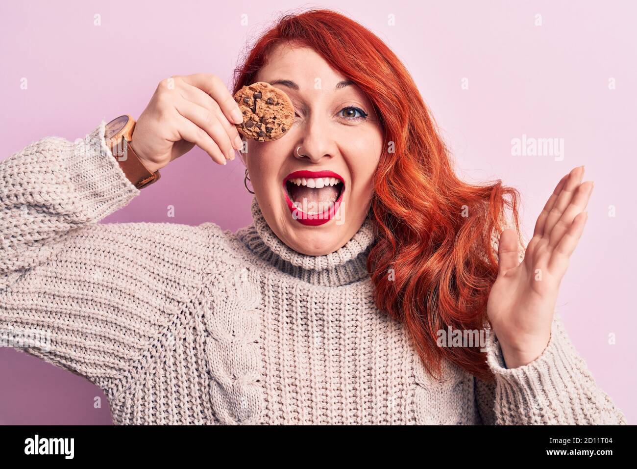 Young beautiful redhead woman standing holding chocolate cookie over ...