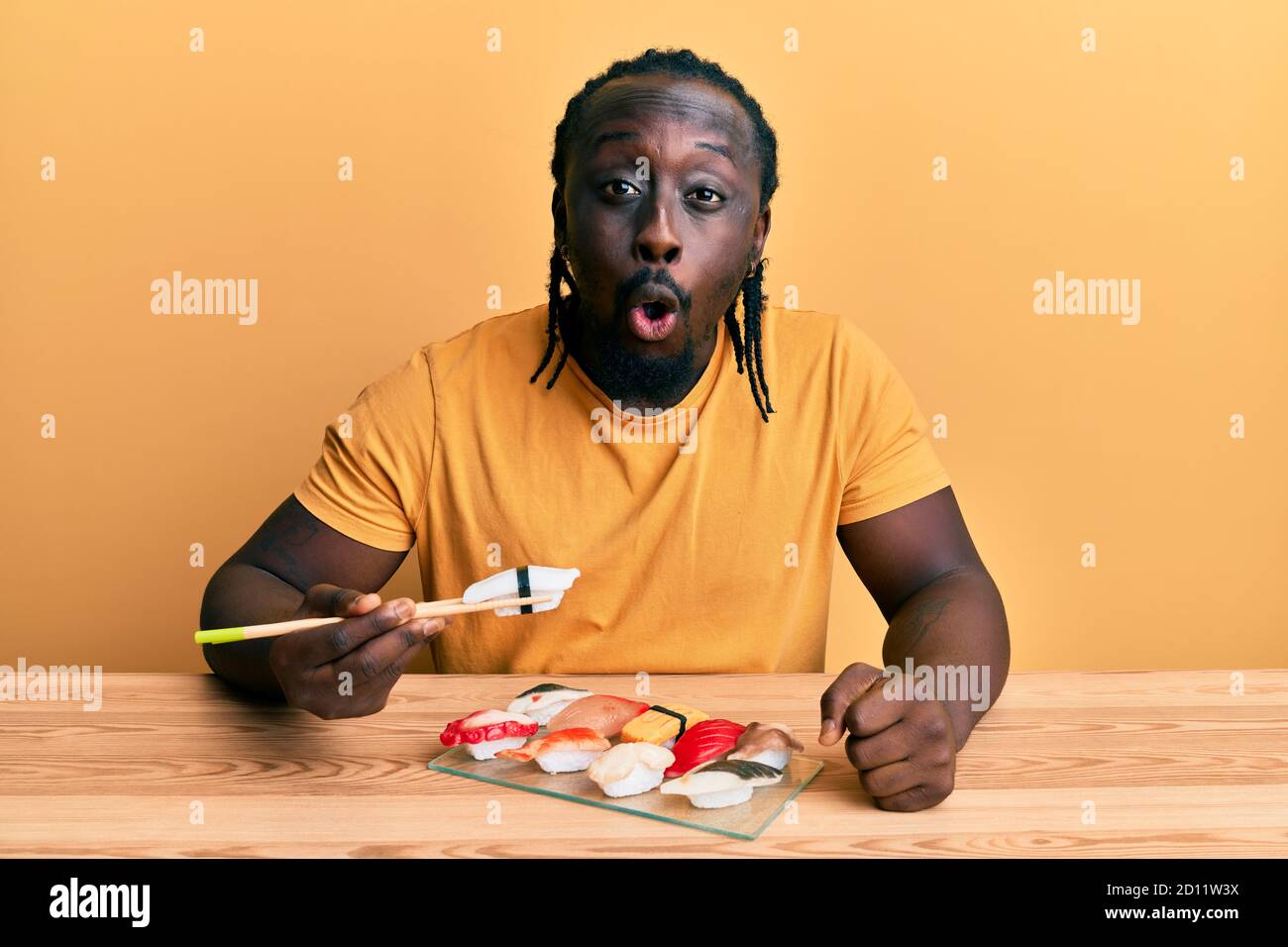 Handsome young black man eating sushi sitting on the table scared and ...
