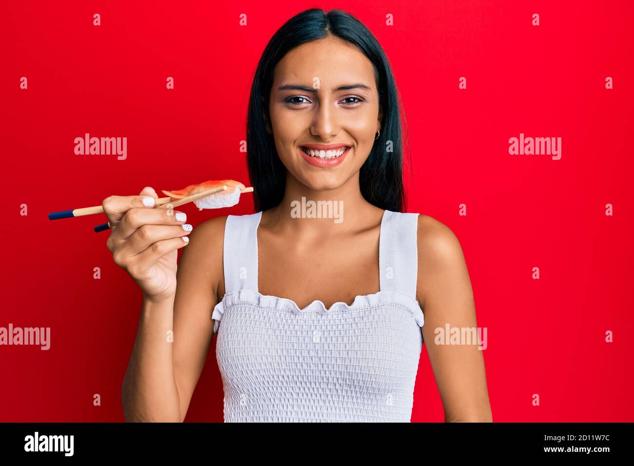 Young brunette woman eating prawn sushi using chopsticks looking ...