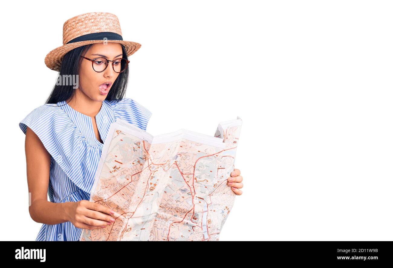 Young beautiful latin girl wearing summer hat holding map scared and amazed with open mouth for ...
