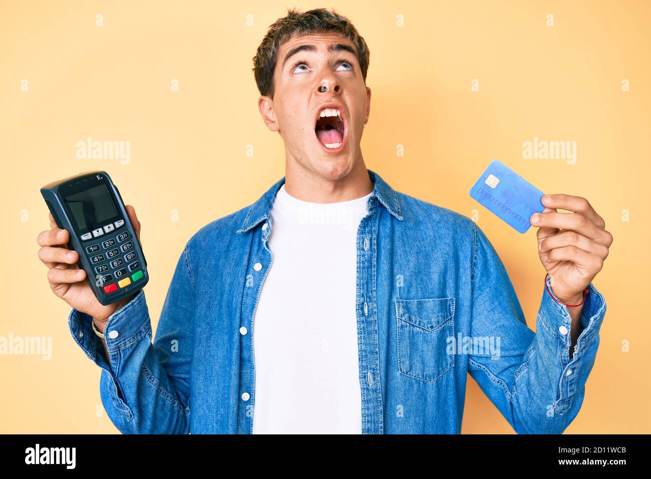 Young handsome man holding credit card and dataphone angry and mad ...