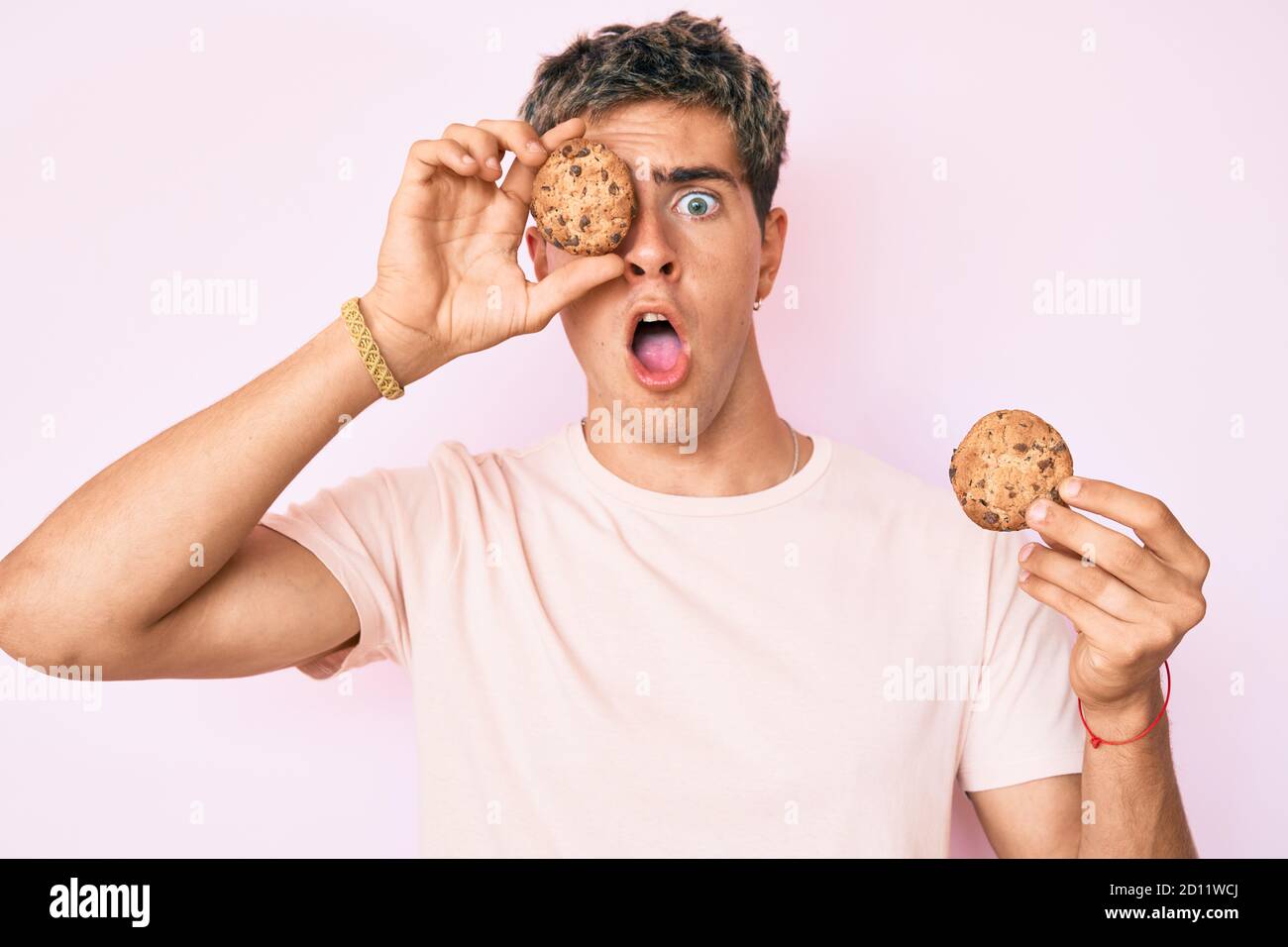 Young handsome man holding cookie afraid and shocked with surprise and ...