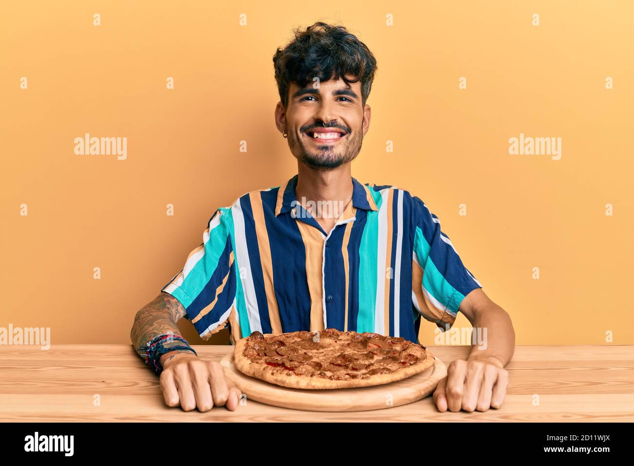 Young hispanic man eating italian pizza sitting on the table looking ...