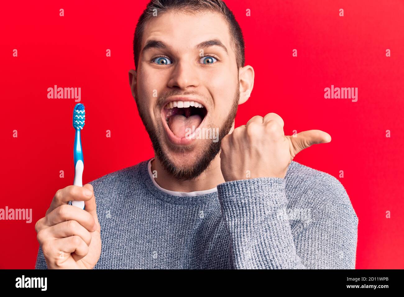 Young handsome man holding toothbrush pointing thumb up to the side ...