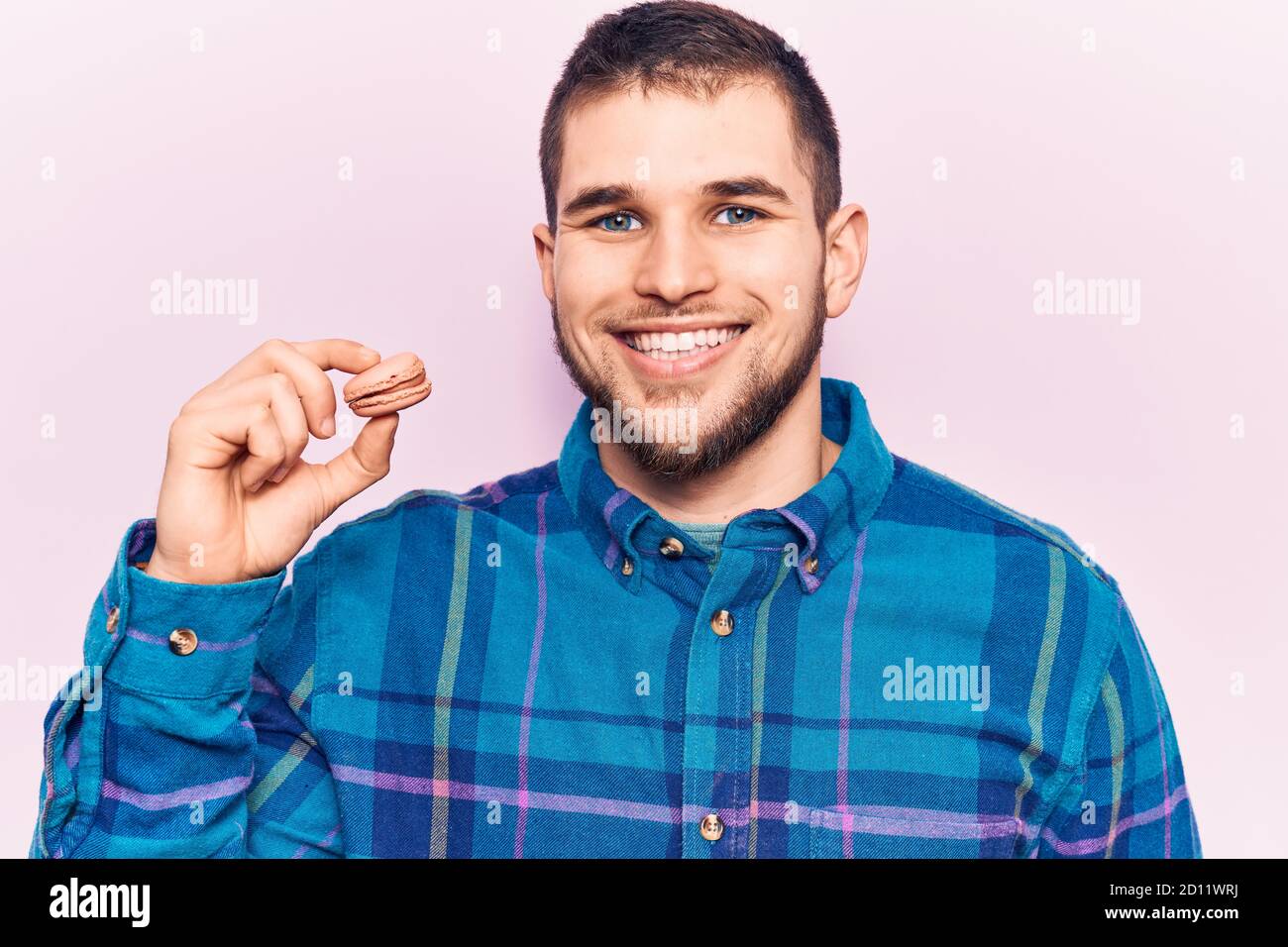 Young handsome man holding chocolate macaron looking positive and happy ...