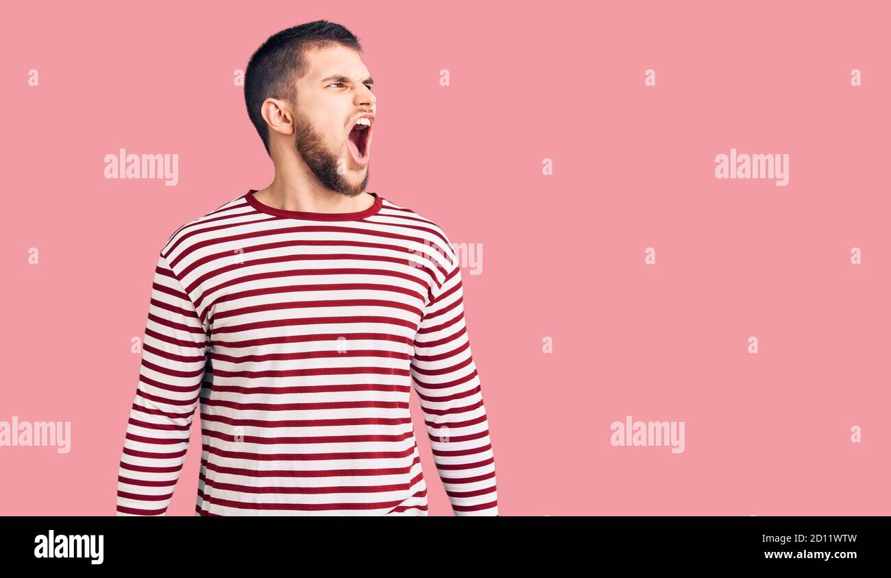 Young handsome man wearing striped sweater angry and mad screaming ...
