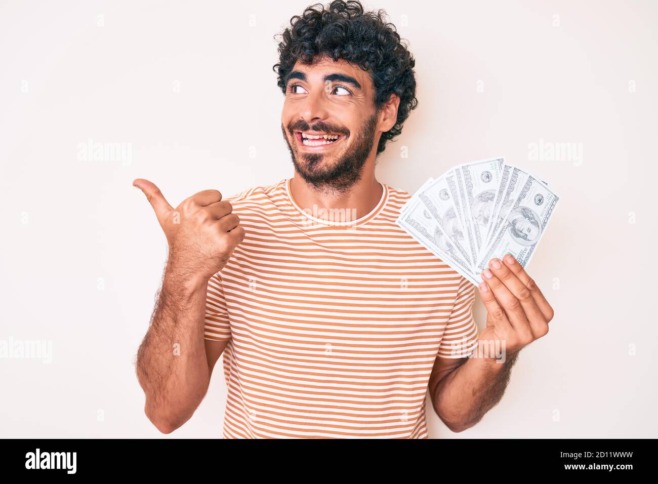 Handsome young man with curly hair and bear holding money bag with ...