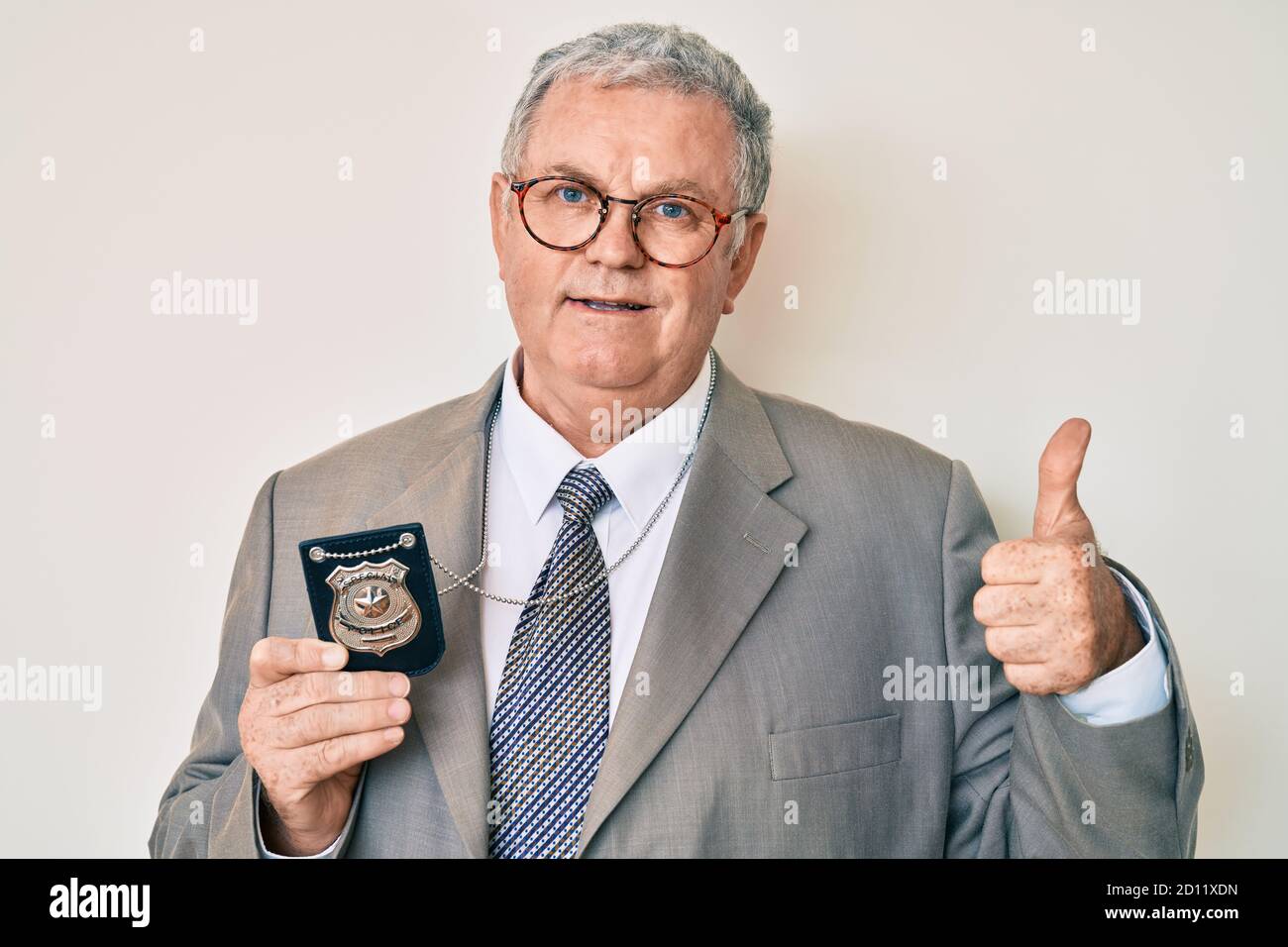 Senior grey-haired man holding detective badge smiling happy and ...