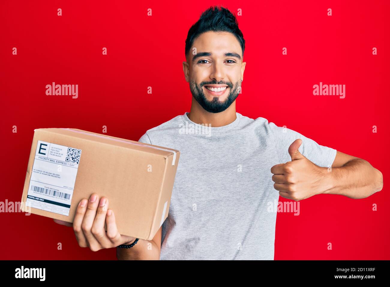 Young man with beard holding delivery package smiling happy and ...