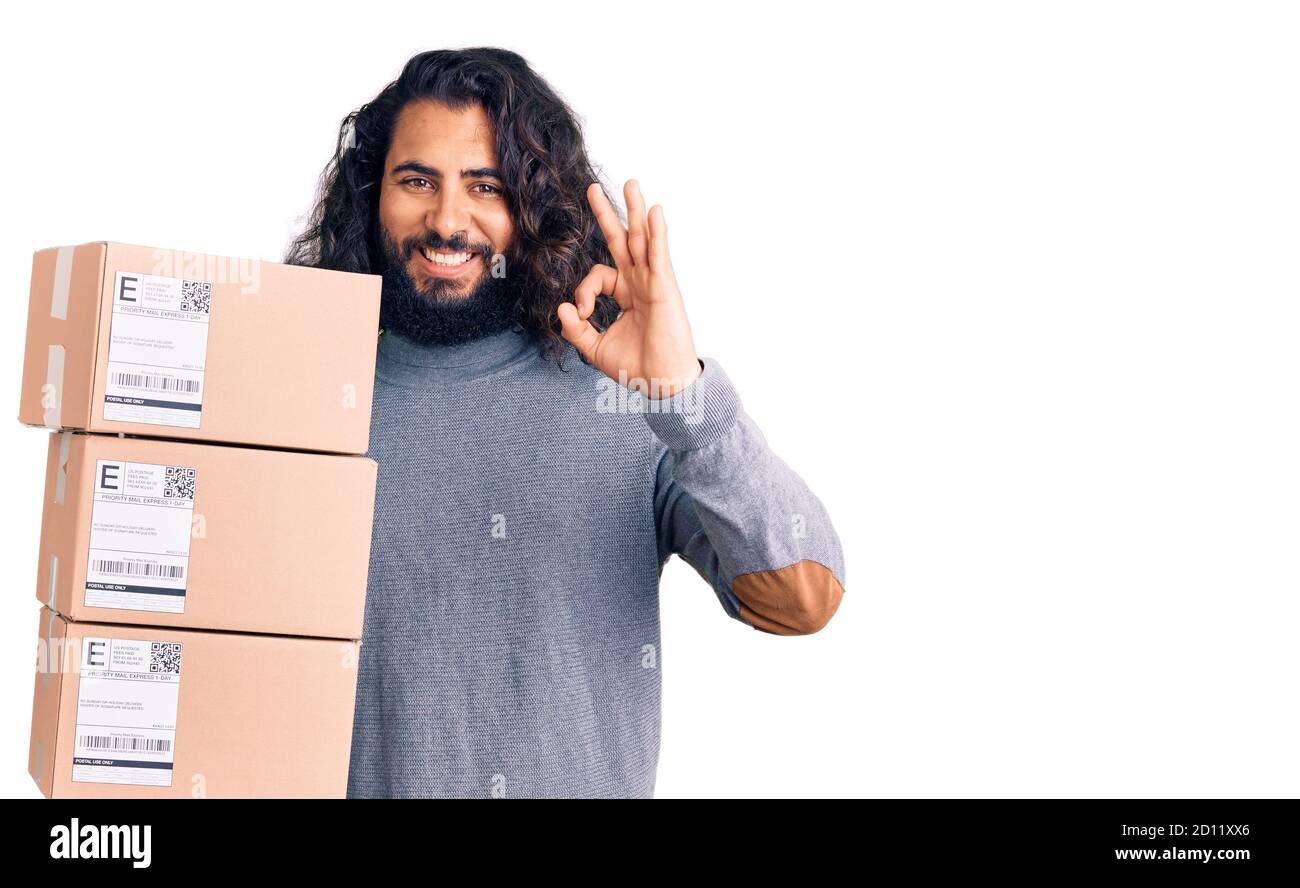Young arab man holding delivery package doing ok sign with fingers ...