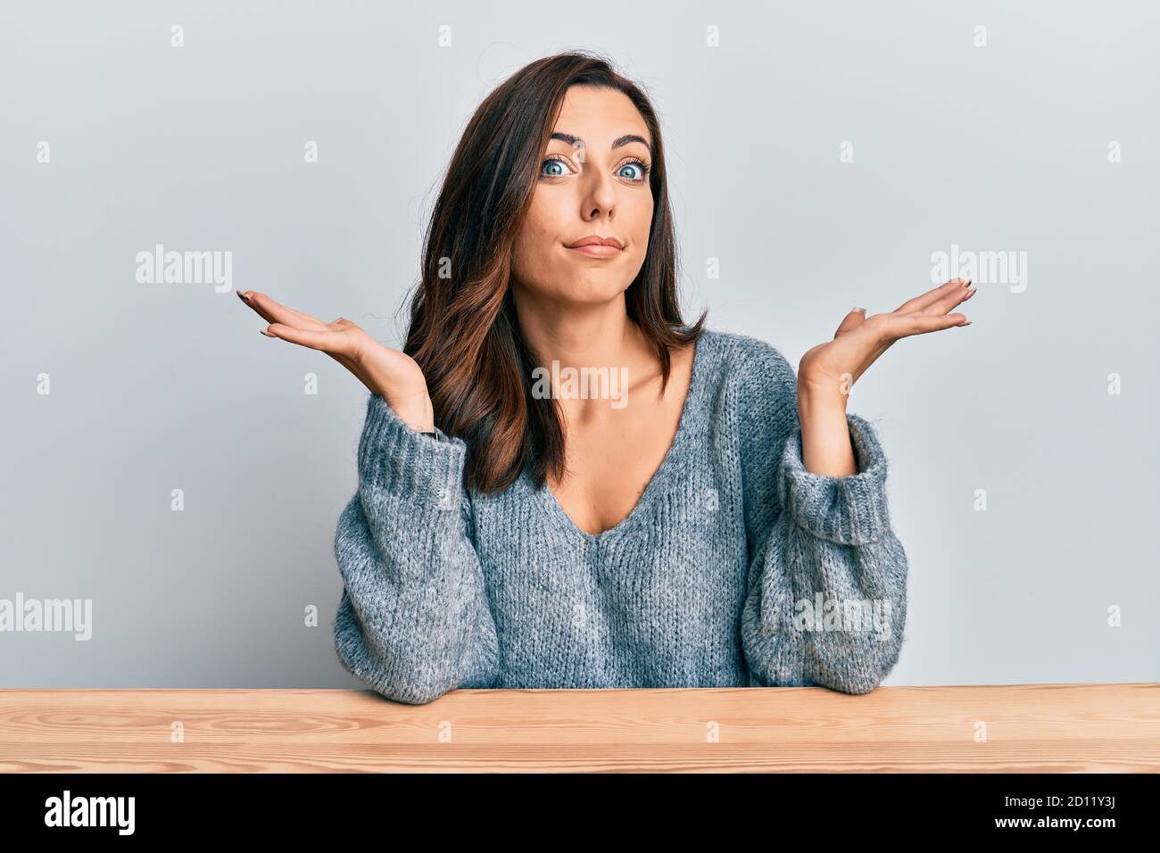 Young brunette woman wearing casual sweater sitting on the table ...