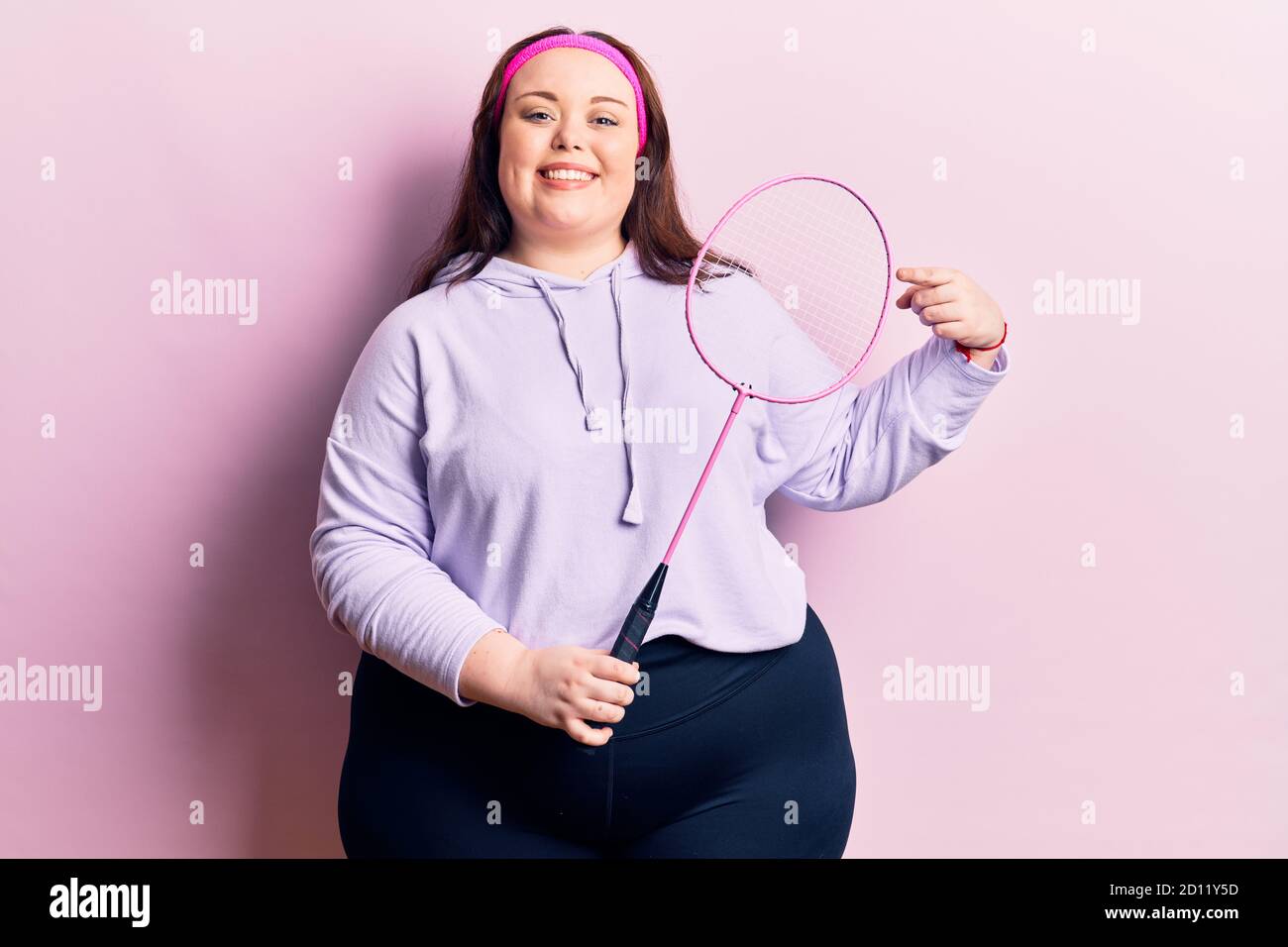 Young plus size woman holding badminton racket smiling happy pointing ...