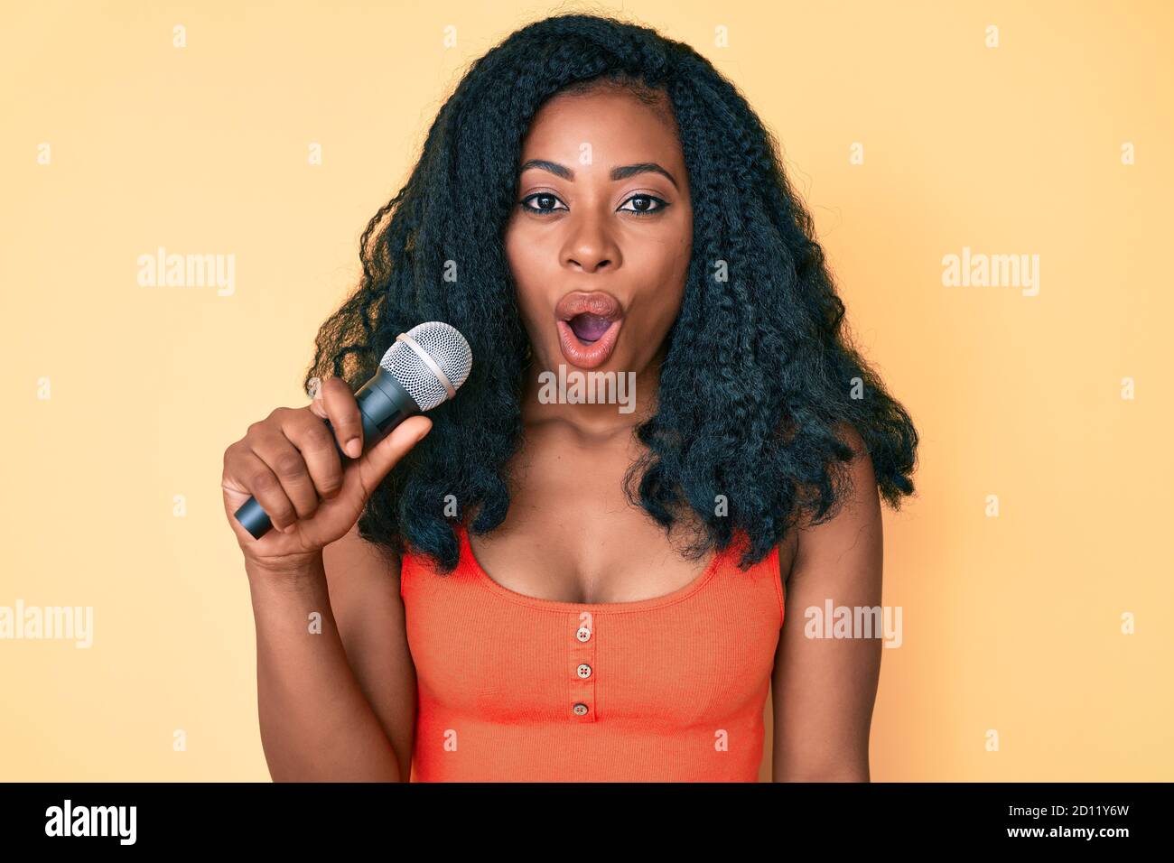 Beautiful african woman singing song using microphone scared and amazed ...