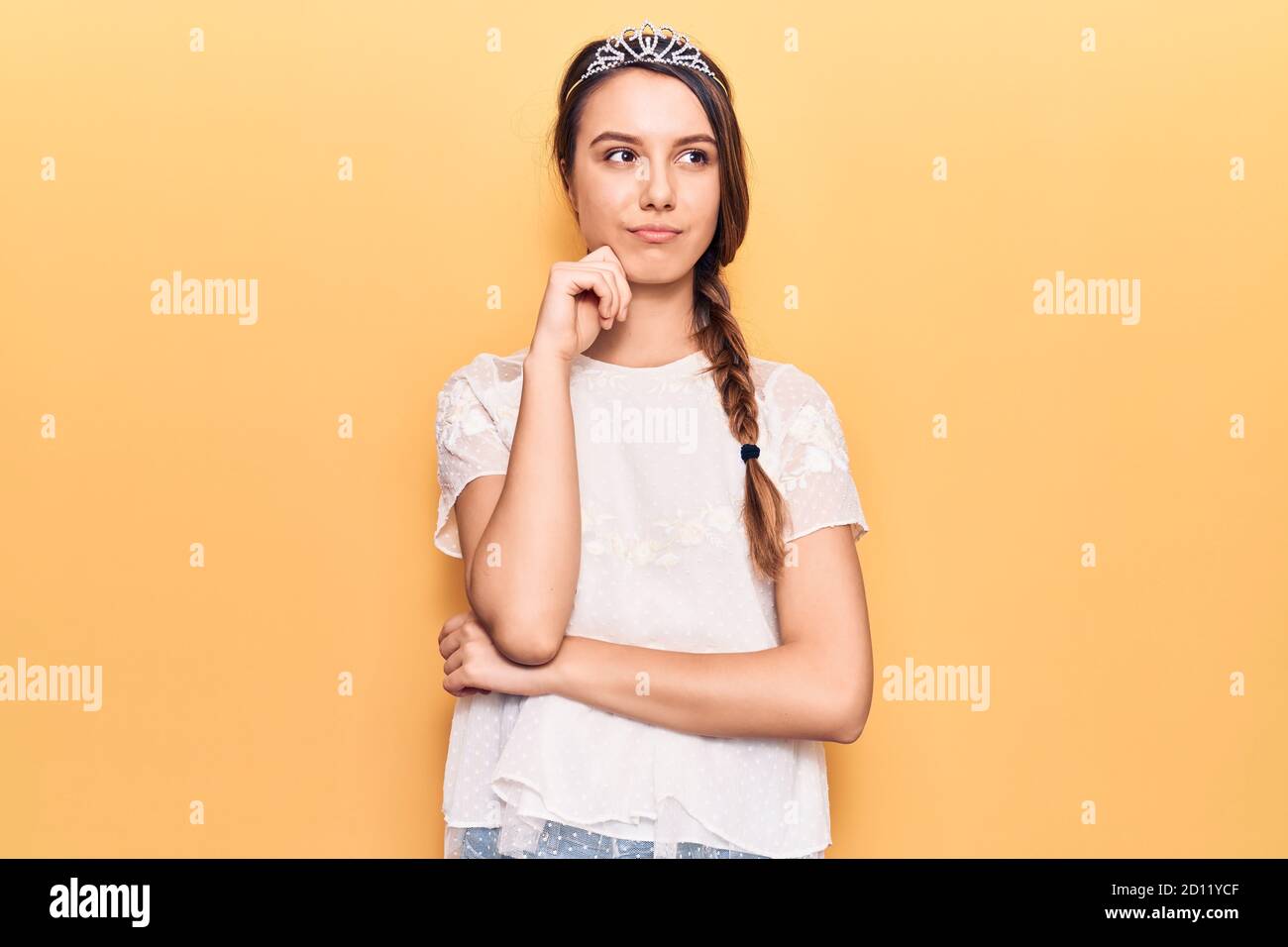 Young beautiful girl wearing crown princess thinking concentrated about ...