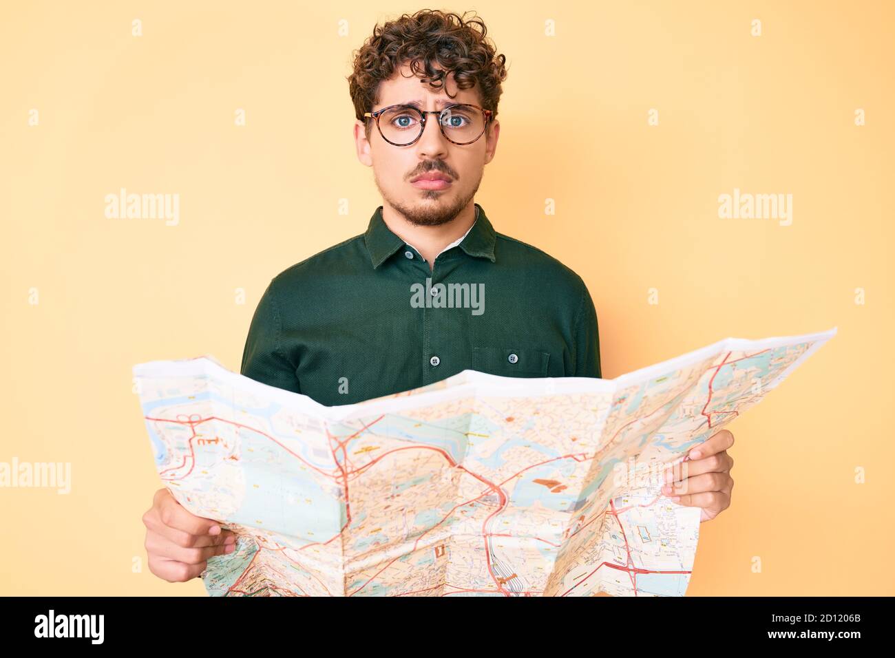 Young caucasian man with curly hair holding city map depressed and ...