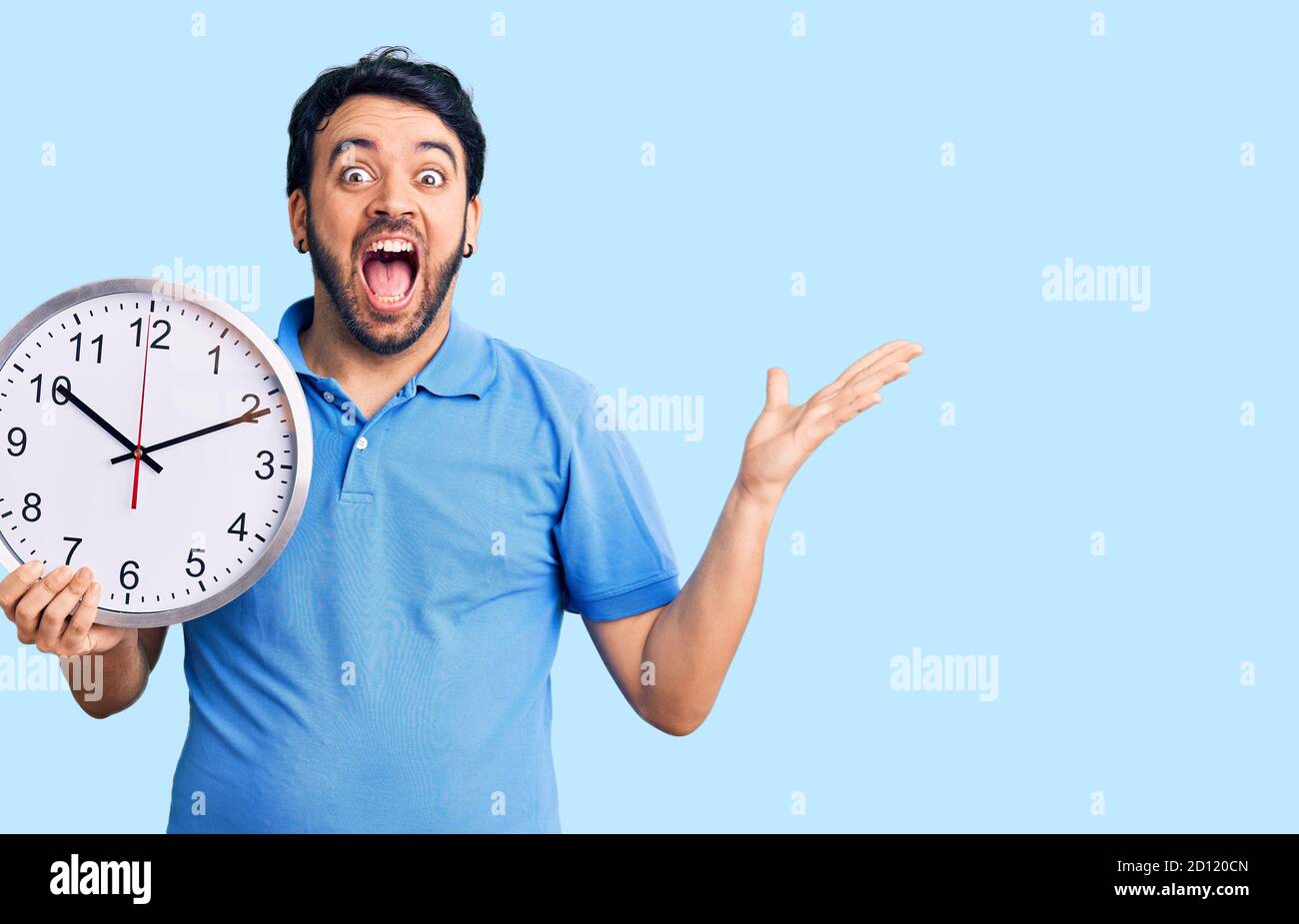 Young hispanic man holding big clock celebrating victory with happy ...