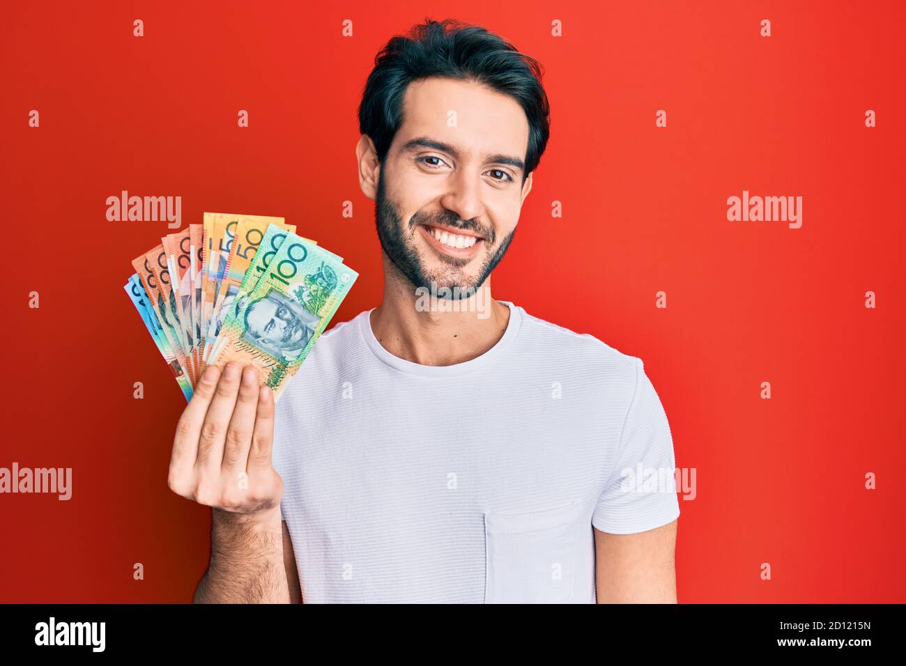 Young hispanic man holding australian dollars looking positive and ...