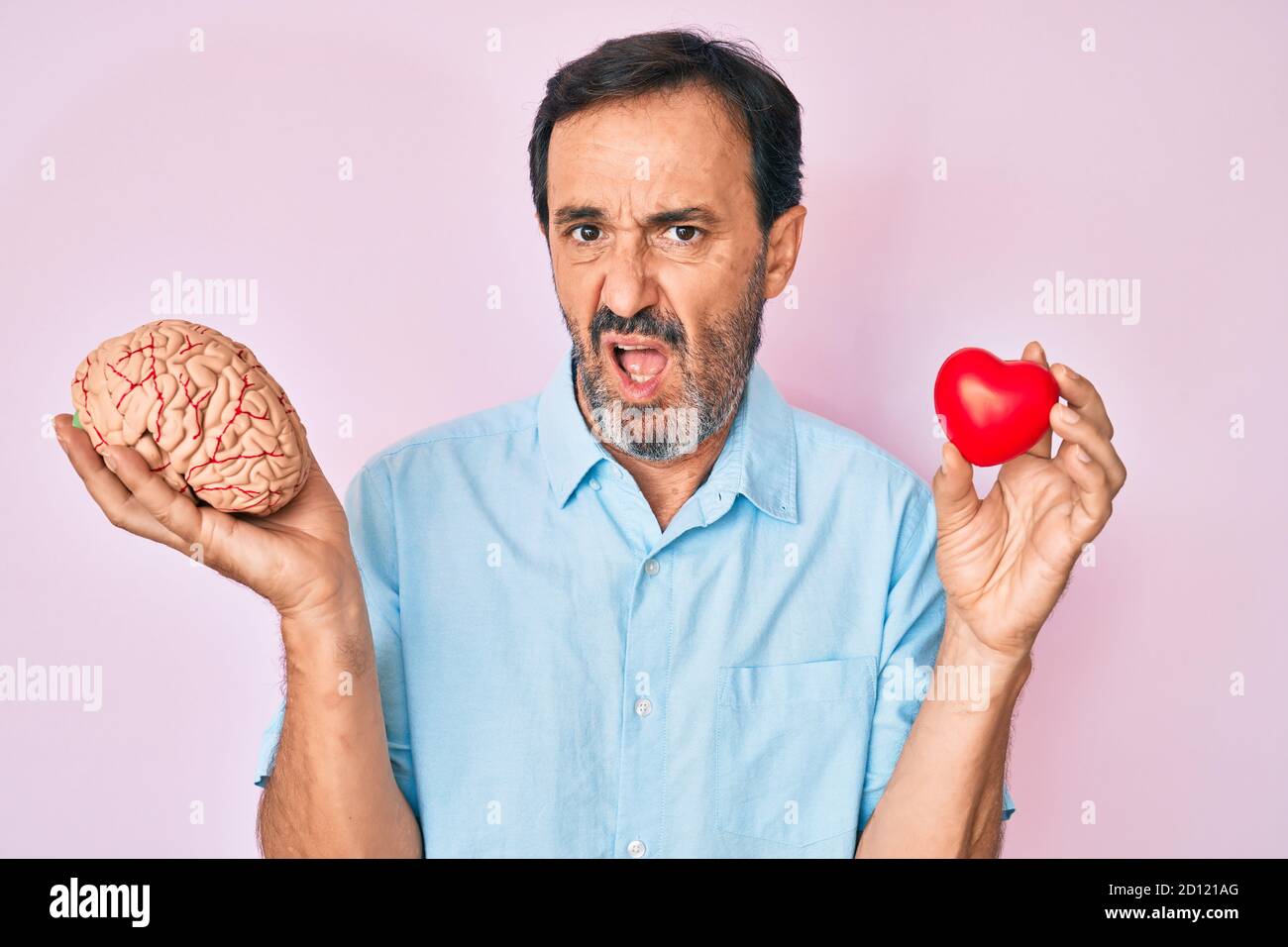 Middle age hispanic man holding brain and heart clueless and confused ...