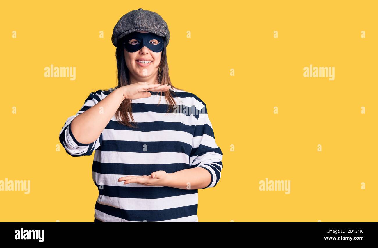 Young beautiful brunette woman wearing burglar mask gesturing with ...