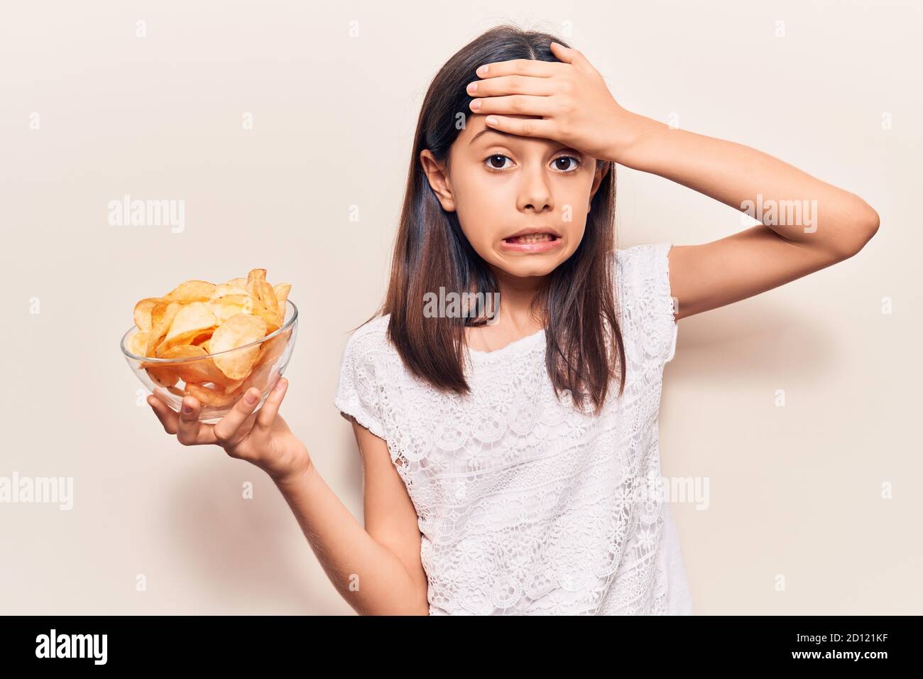 Beautiful child girl holding potato chip stressed and frustrated with ...