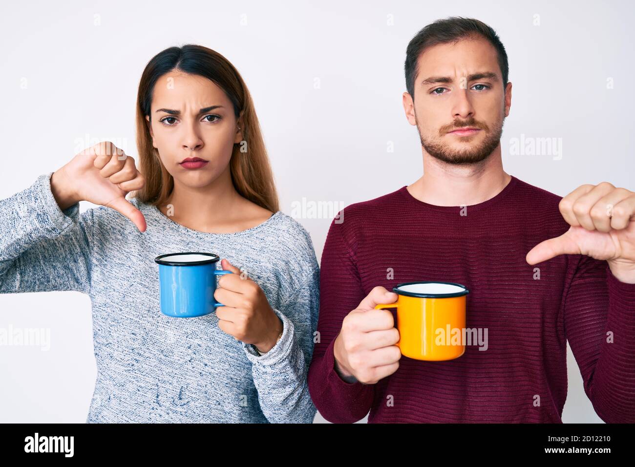 Beautiful couple holding coffee with angry face, negative sign showing ...