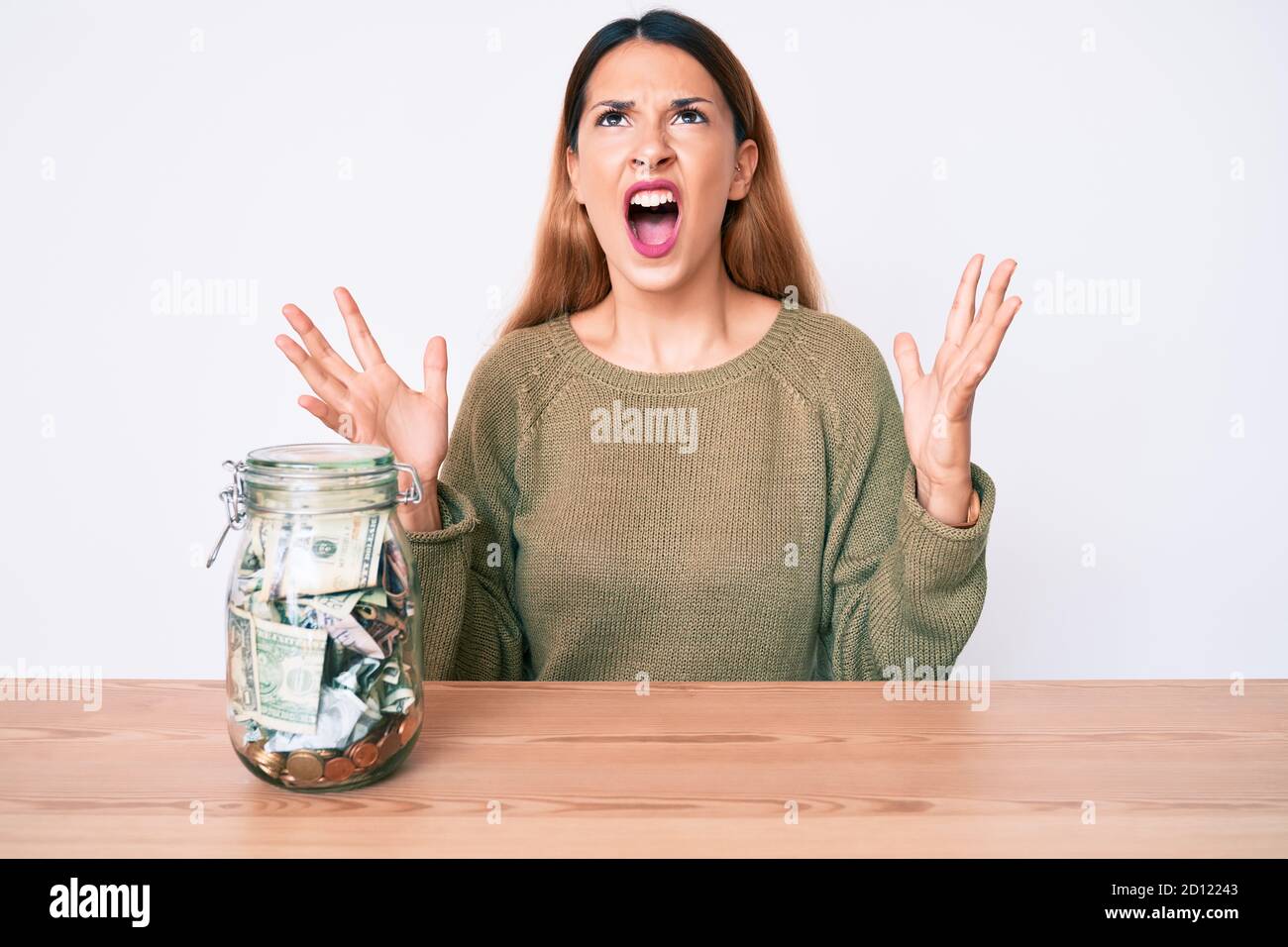 Young brunette woman sitting on the table with jar full of dollars ...