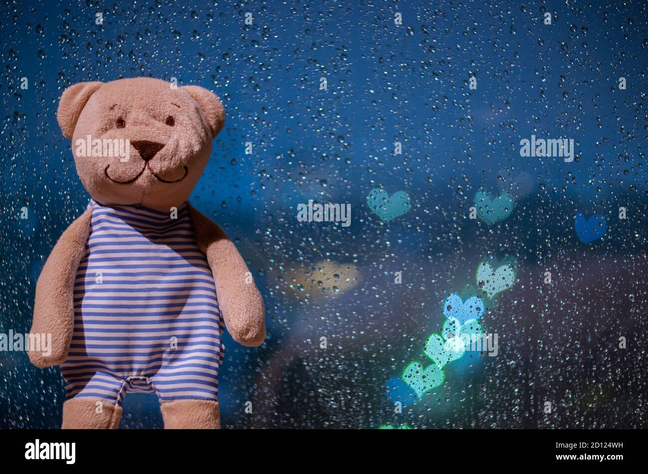 Teddy bear standing at window when raining with colorful love shape ...
