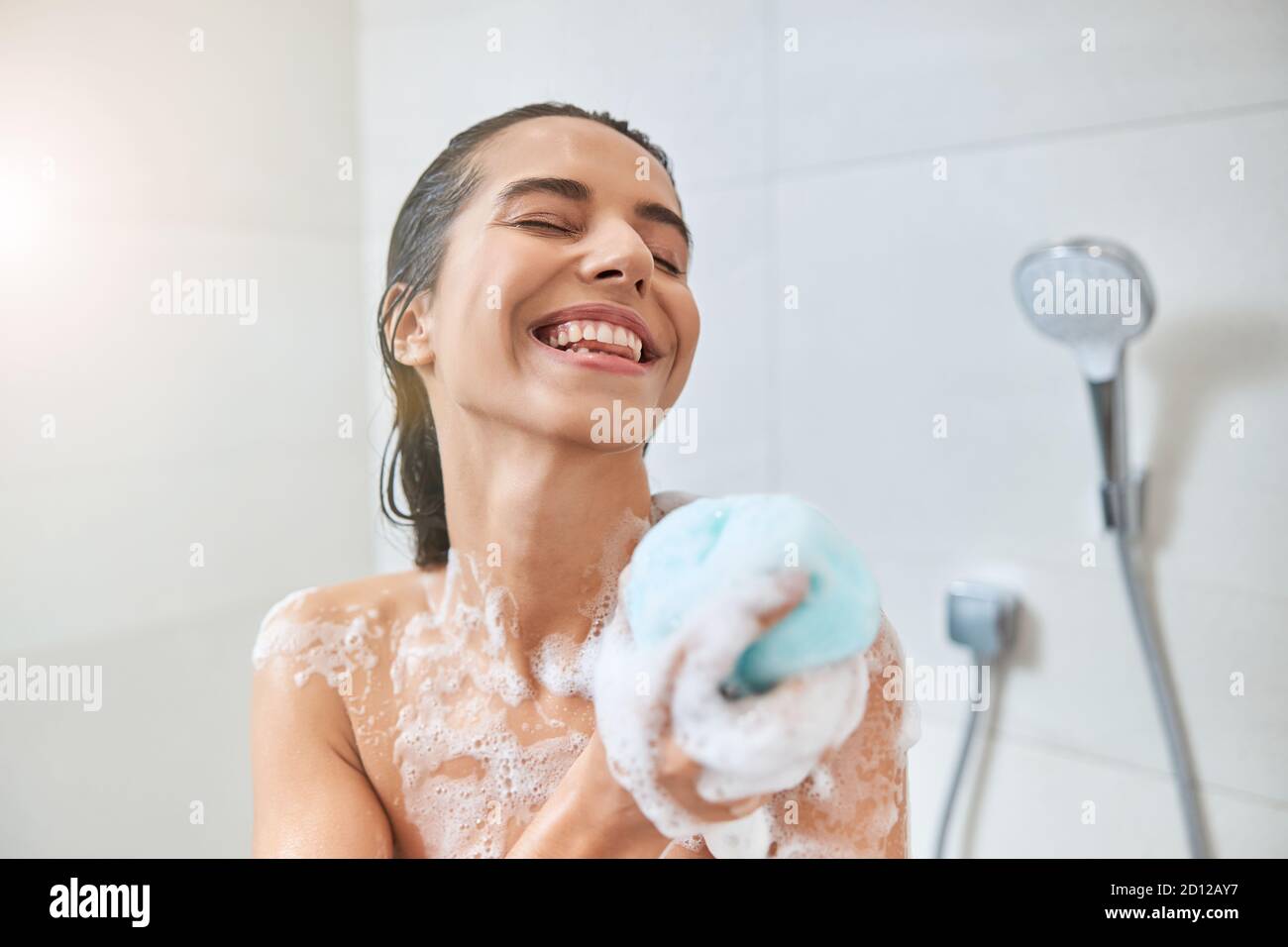 Smiling young woman washing body with bath loofah Stock Photo - Alamy