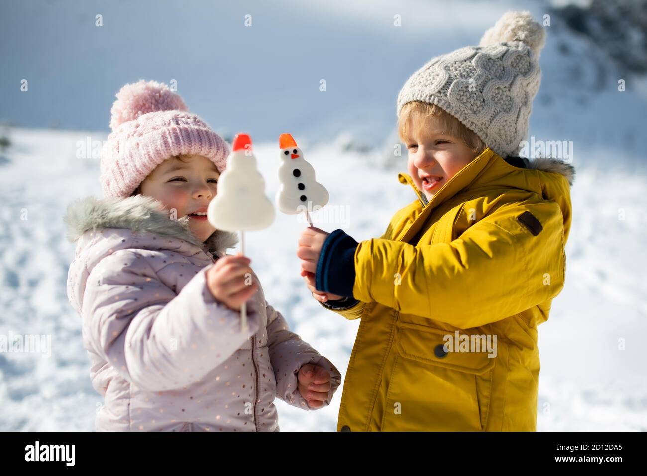 Two small children standing in snow in winter nature, eating sweets ...