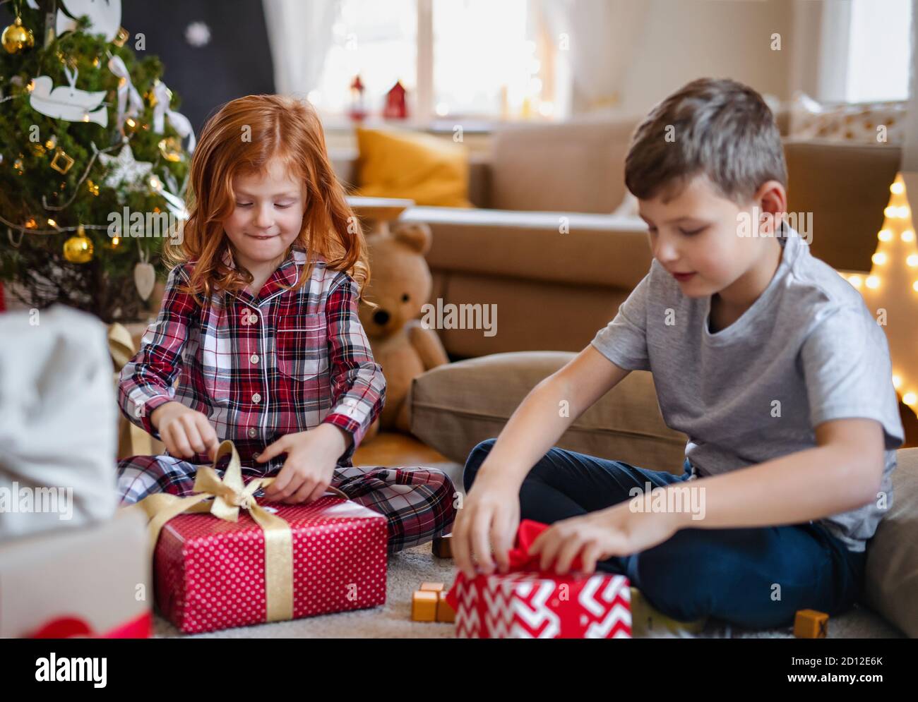 Small girl and boy in pajamas indoors at home at Christmas, opening ...