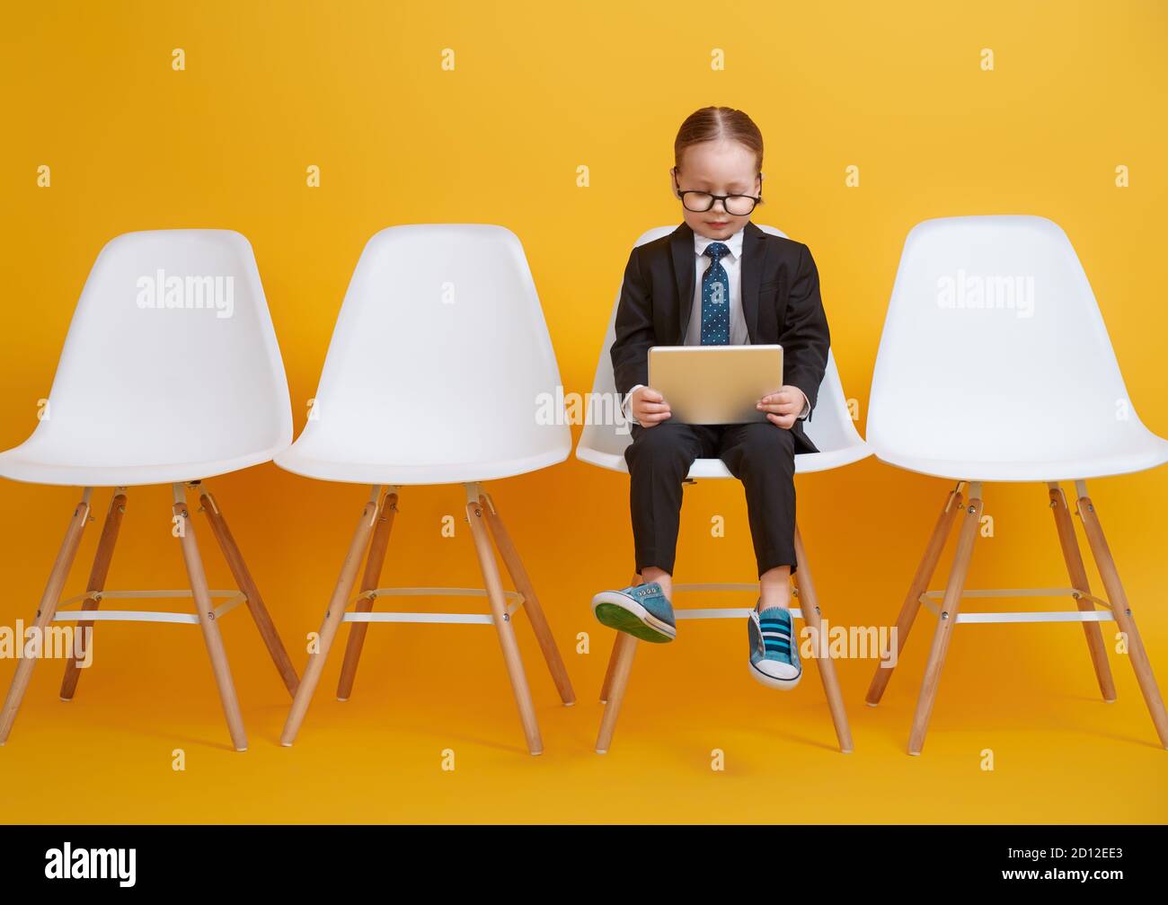 Cute baby girl working on a tablet on bright yellow wall background ...