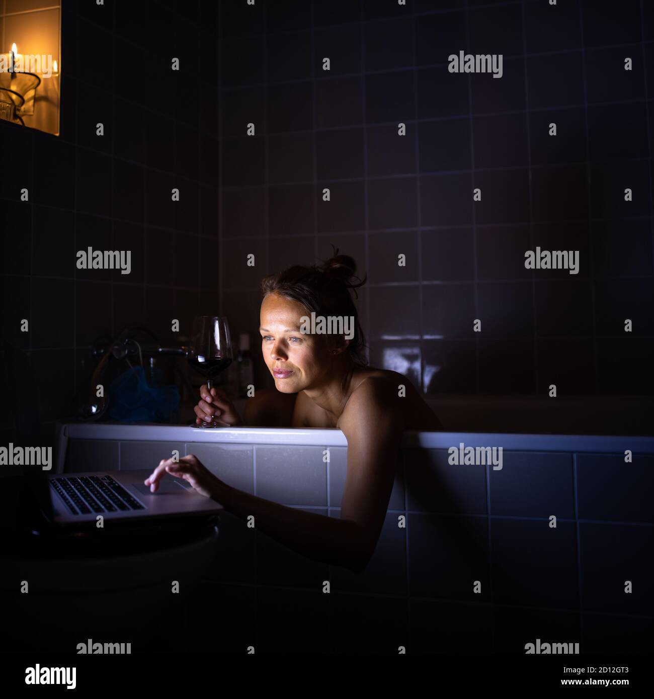 Young woman taking a bath, drinking red wine, enjoying a movie ...