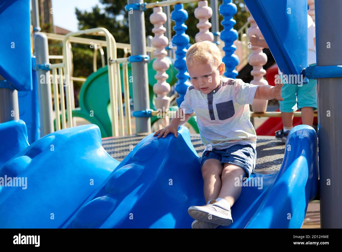A small caucasian boy slides down a slide in the playground Stock Photo ...