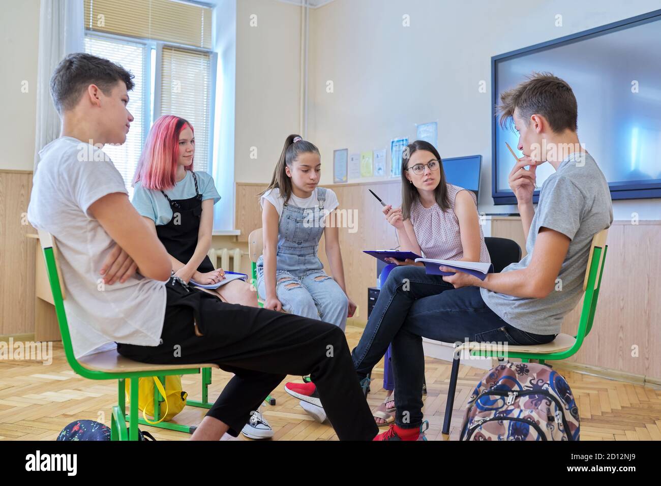 Group of teenagers with teacher at classroom, sitting talking ...